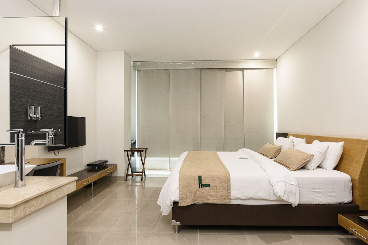 Quarto de hotel moderno com uma cama grande, uma toucador com espelho, uma TV de tela plana e um closet espaçoso.