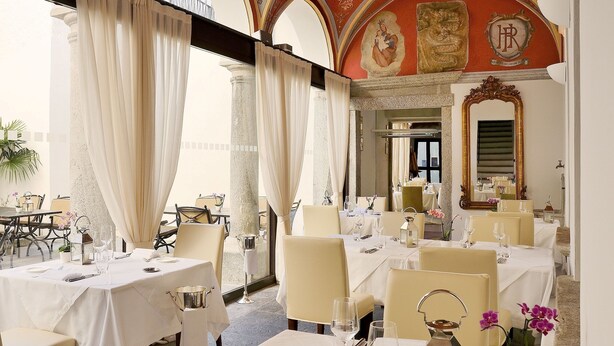 Um restaurante com várias mesas preparadas para refeições, com toalhas de mesa brancas e cadeiras.