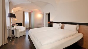 Quarto de hotel com uma cama grande, uma cadeira, uma mesa com abajur e um guarda-roupa.