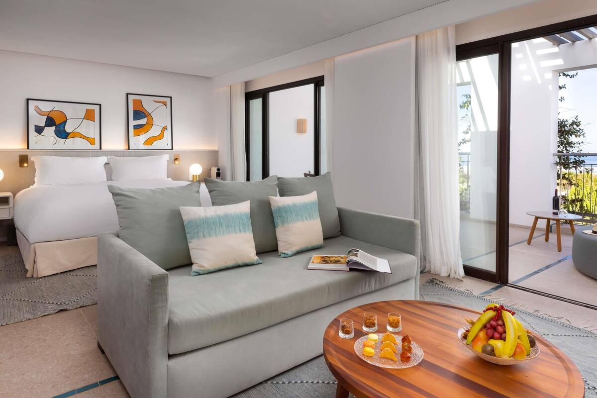 Quarto de hotel moderno com cama, sofá e varanda.