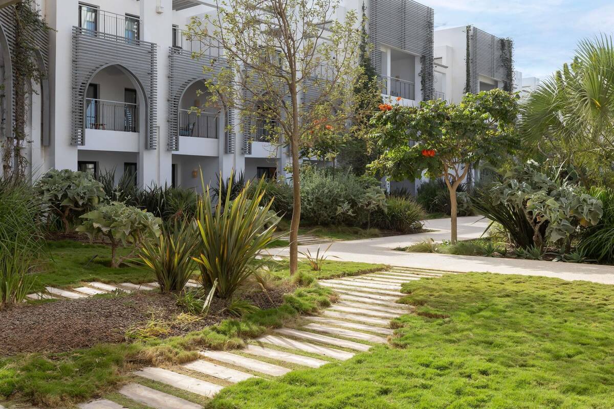 Um edifício moderno com várias varandas, rodeado por jardins bem cuidados e um caminho amplo.