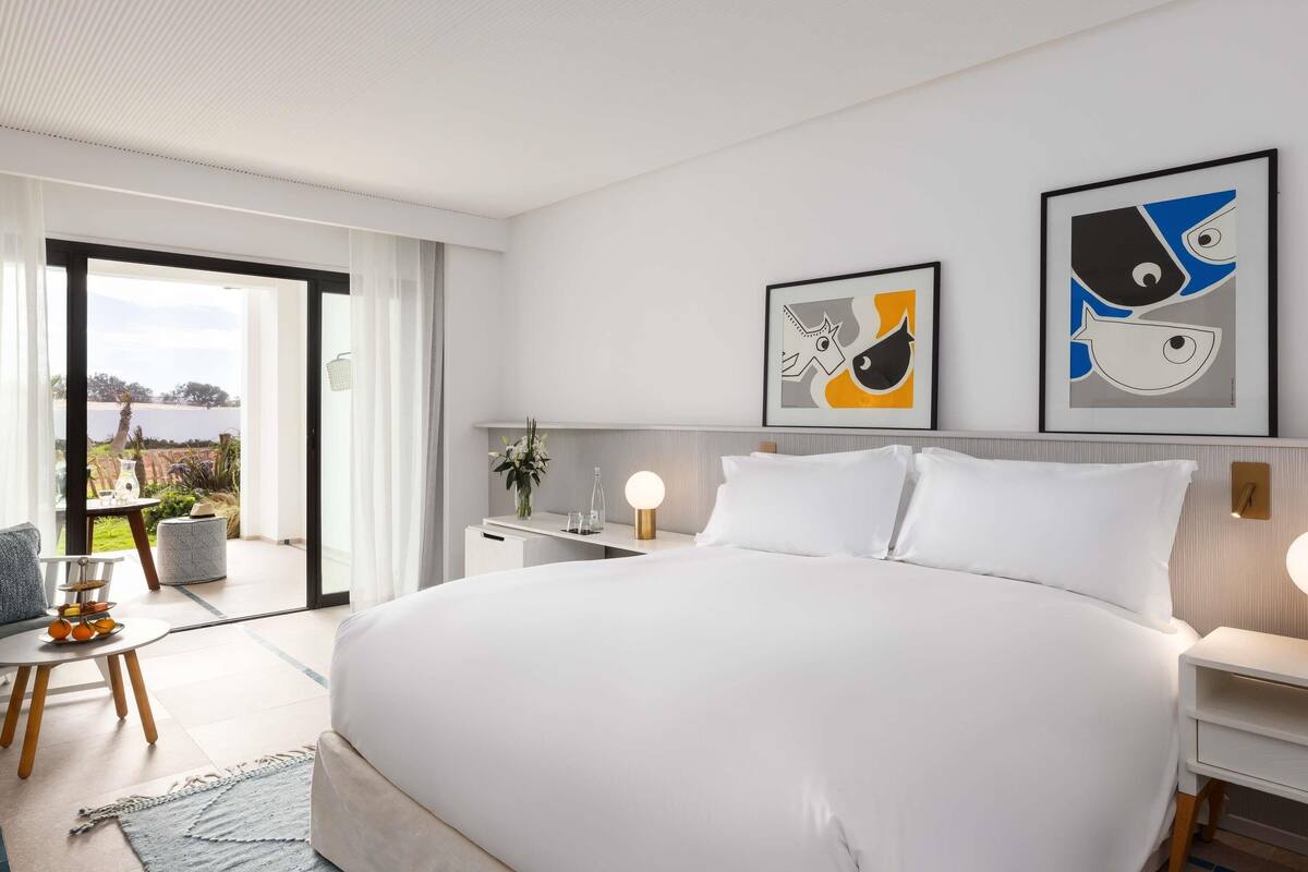 Quarto de hotel moderno com uma cama grande, uma escrivaninha, uma cadeira e obras de arte nas paredes.