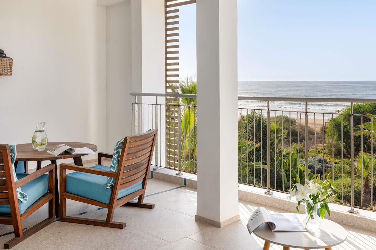 Uma varanda com vista para o oceano, uma mesa com cadeiras e um vaso com flores.
