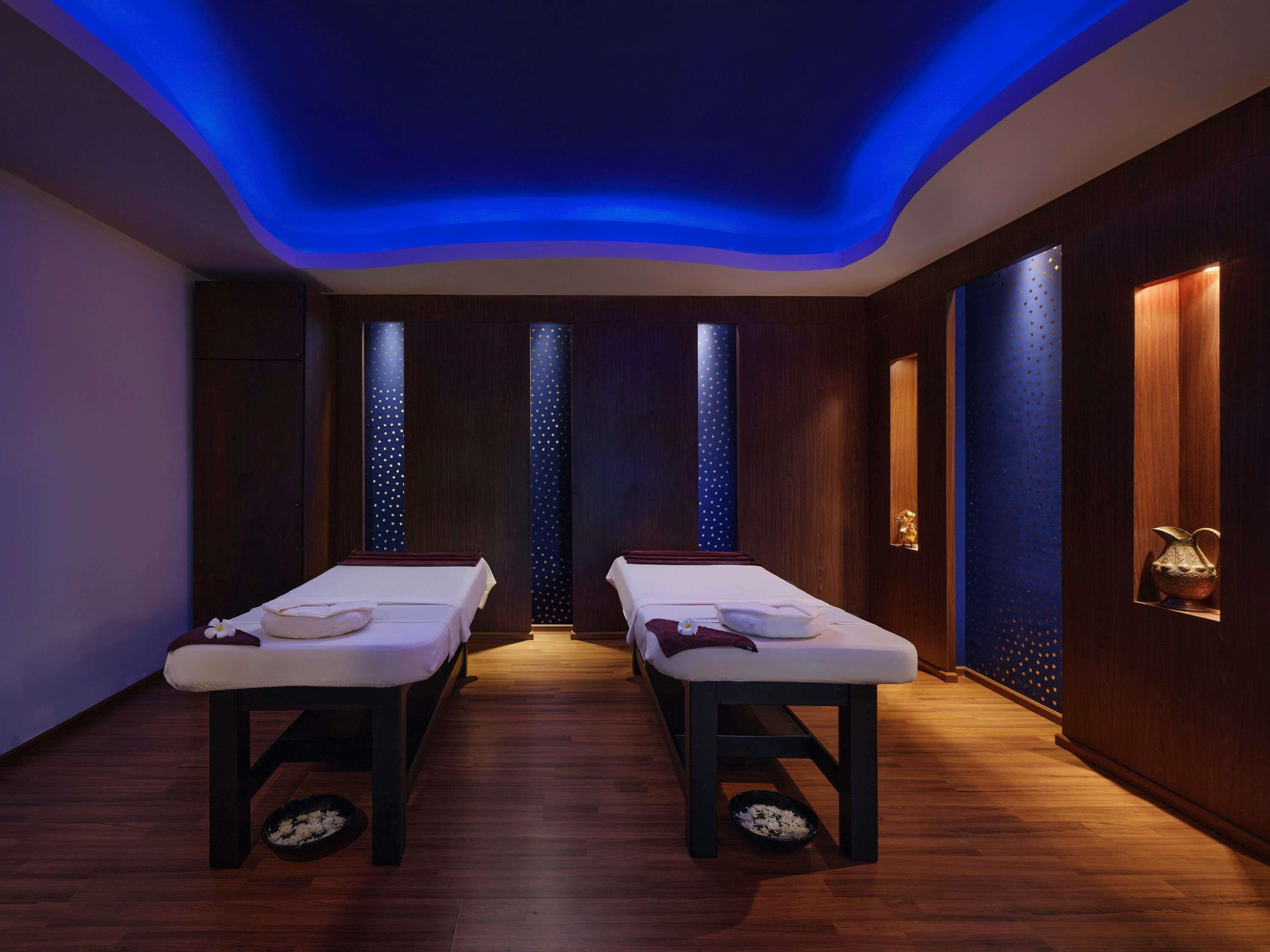 Sala de spa com duas mesas de massagem, piso de madeira e iluminação azul ambiente.