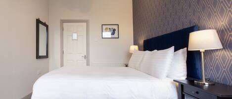 Quarto de hotel com cama, mesas de cabeceira, painel de cabeceira, porta e parede estampada.