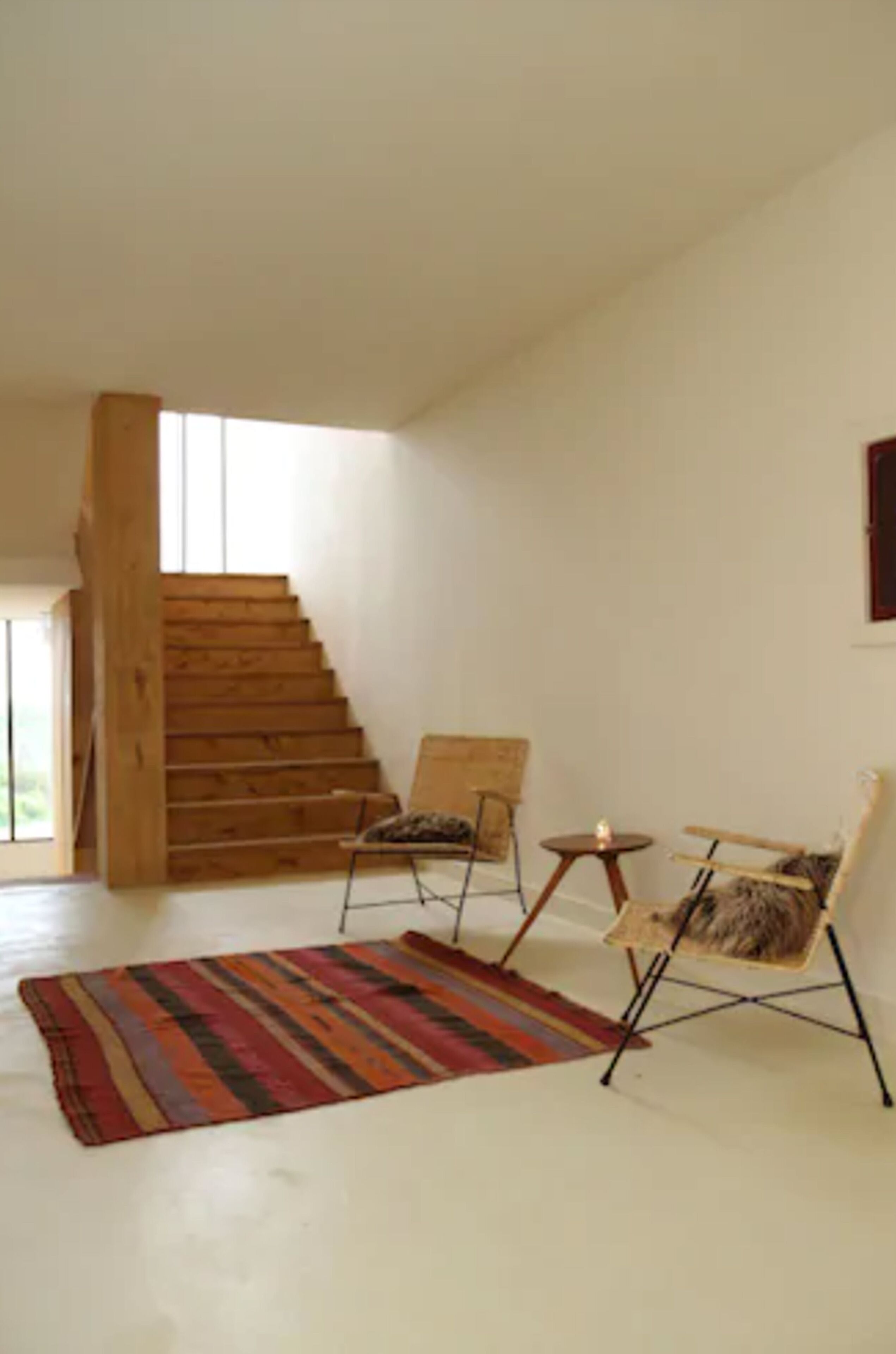 Quarto espaçoso com escada de madeira, duas cadeiras, uma mesa pequena e um tapete colorido.