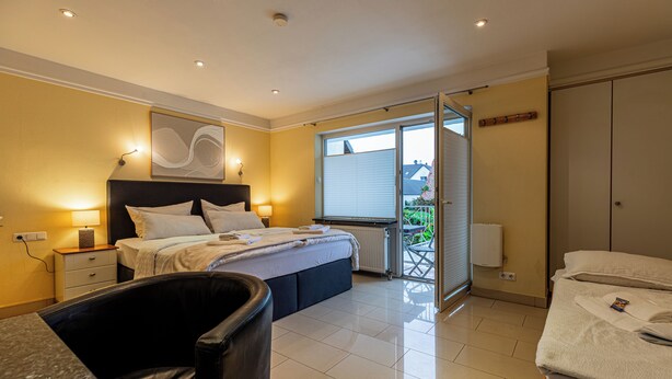 Quarto de hotel com cama, cadeira, escrivaninha, janela e porta para área externa.