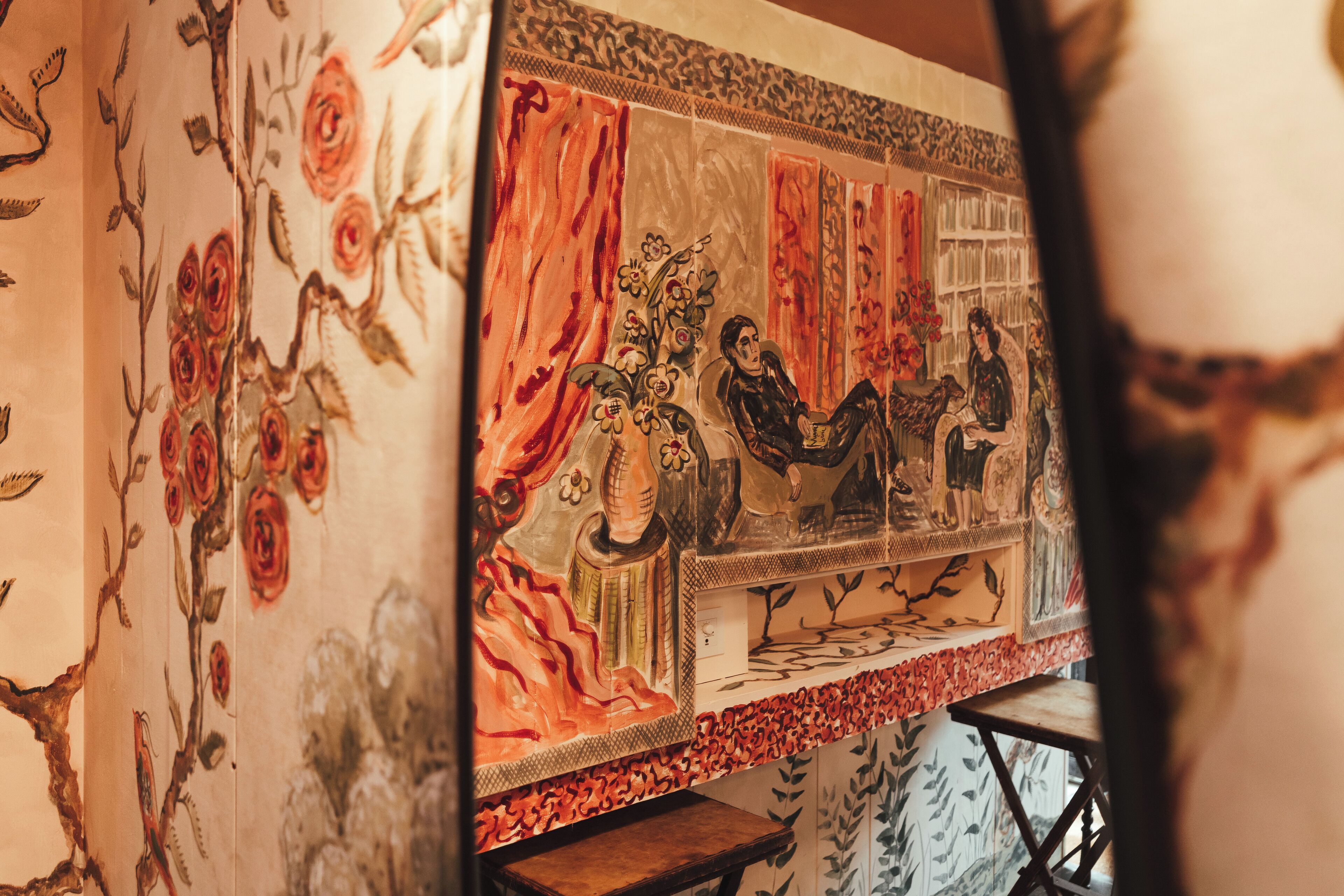 Quarto com um mural retratando uma cena histórica, uma mesa de madeira e uma cadeira.