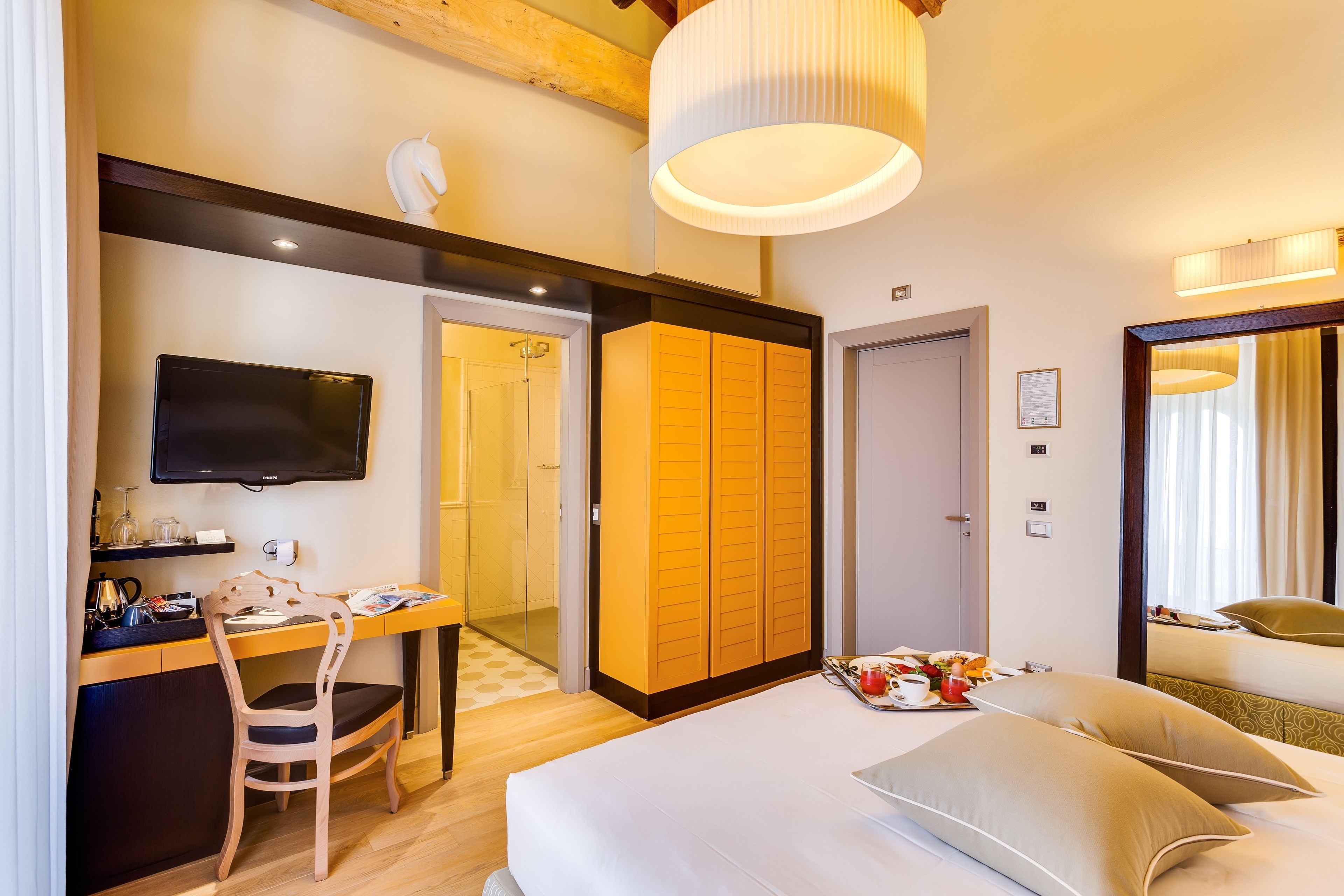 Quarto de hotel com cama, escrivaninha com cadeira, televisão e guarda-roupa.