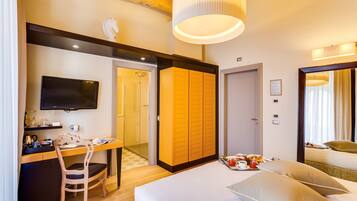Quarto de hotel com cama, escrivaninha com cadeira, televisão e guarda-roupa.