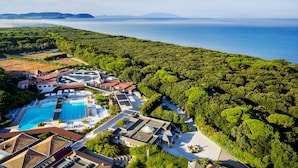Vista aérea de um resort com uma piscina grande, vários edifícios e vegetação exuberante ao redor de uma massa de água.