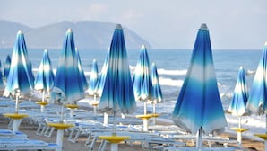 Guarda-sóis e espreguiçadeiras dispostas na areia, com o oceano ao fundo.