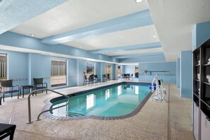 Piscina interna com piso azulejado, escada de piscina e área de estar com cadeiras e mesas.