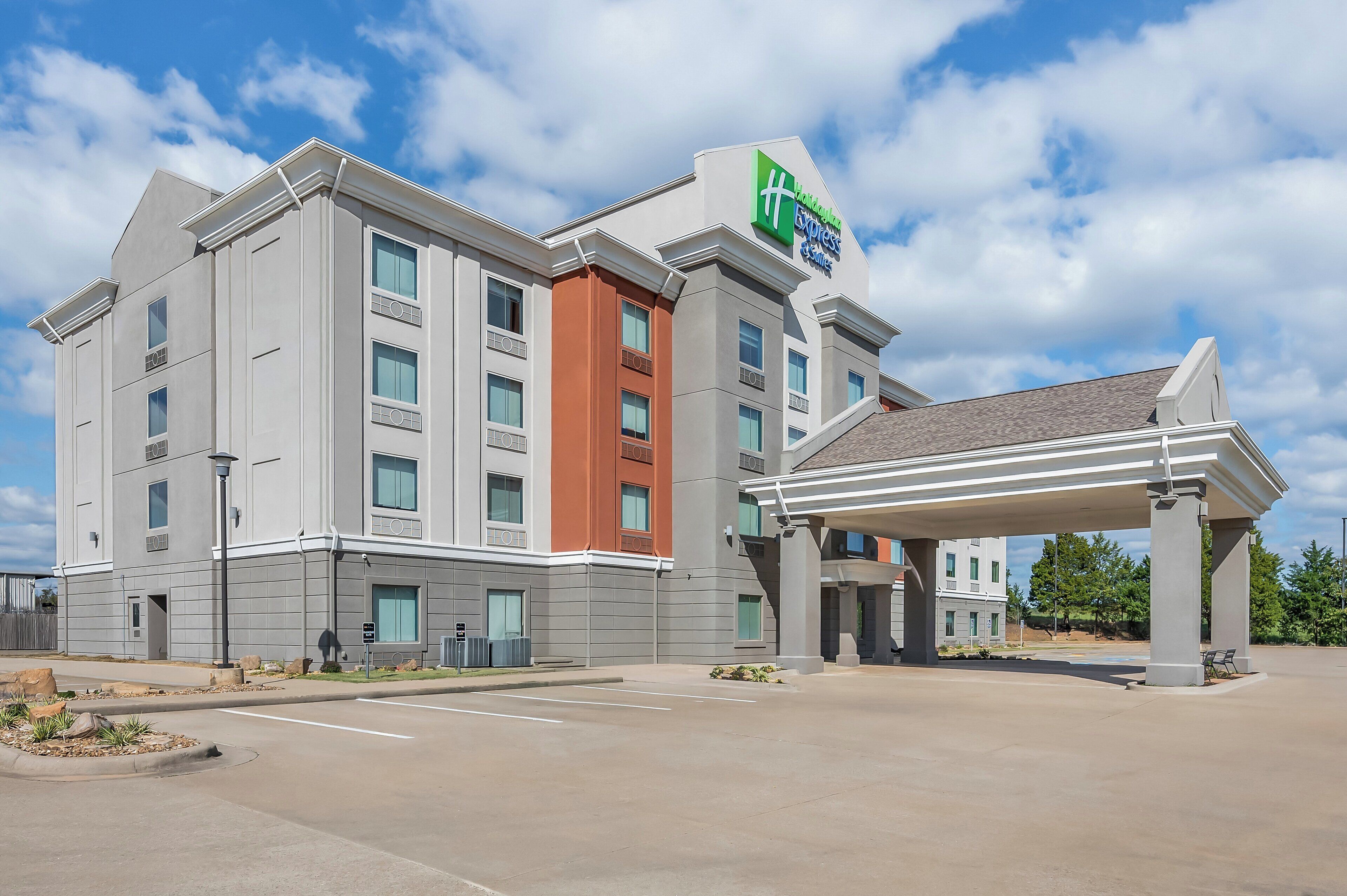 Um hotel moderno com um destaque para a placa 'Holiday Inn Express', uma entrada coberta e um estacionamento.
