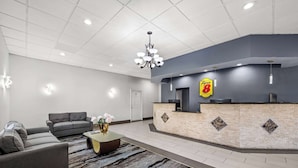 Uma área de recepção com design moderno, com balcão de atendimento, um lustre e um espaço de estar com sofás e uma mesa de centro.