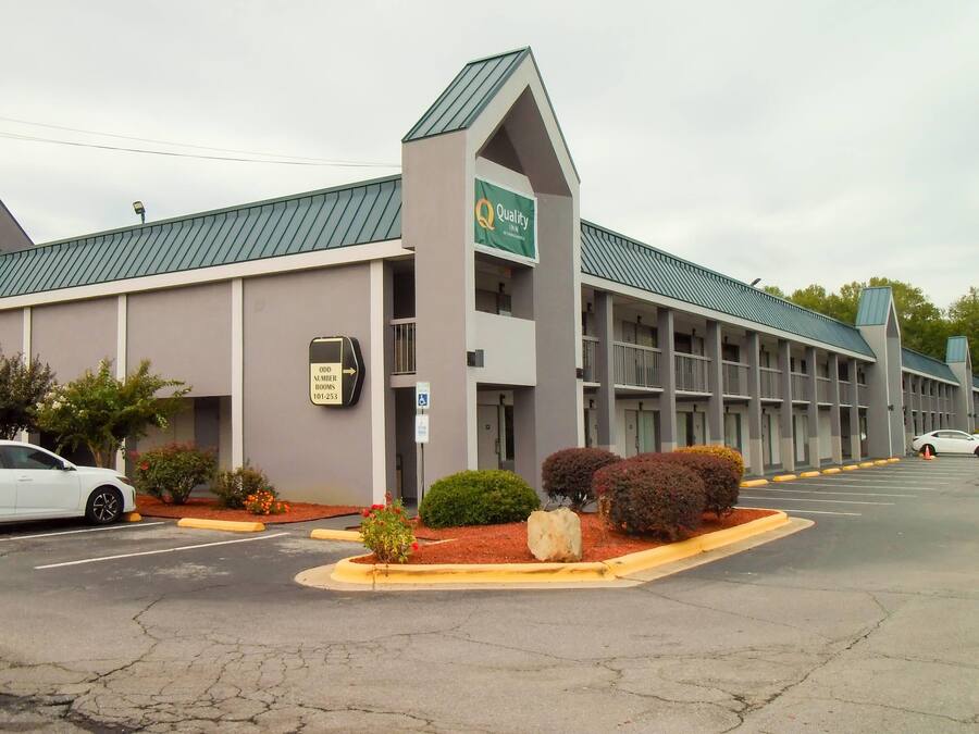 Um motel com teto verde, placa da Quality Inn e estacionamento com carros.