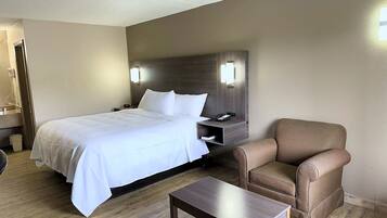 Quarto de hotel com cama, mesa de cabeceira, cadeira e uma pequena mesa.