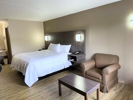 Quarto de hotel com cama, mesa de cabeceira, cadeira e uma pequena mesa.