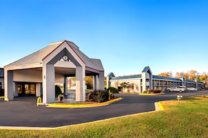 Um hotel com telhado triangular característico, entrada coberta e estacionamento.