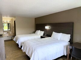 Quarto de hotel com duas camas, uma escrivaninha, um espelho e uma mesa de cabeceira com abajur.