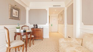 Quarto de hotel com área de refeições, incluindo uma mesa e cadeiras de madeira, um sofá e um tapete estampado.