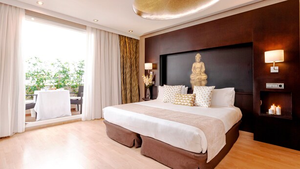 Quarto de hotel moderno com uma cama grande, uma estátua na parede e vista para o verde lá fora.