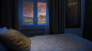 Quarto com cama, janela com vista para a paisagem urbana e quadro pendurado na parede.