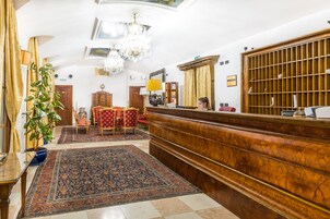 Uma área de recepção com um balcão de mármore, um candelabro, um tapete grande e uma planta.