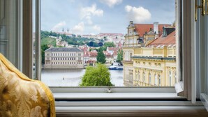 Quarto com vista para a paisagem urbana através de uma janela, uma mesa de madeira e uma cadeira estampada.