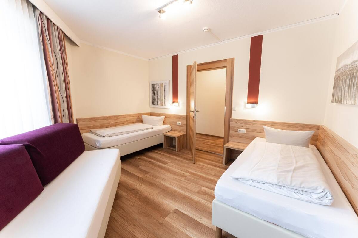 Quarto de hotel com duas camas, um sofá, piso de madeira e uma porta com espelho.
