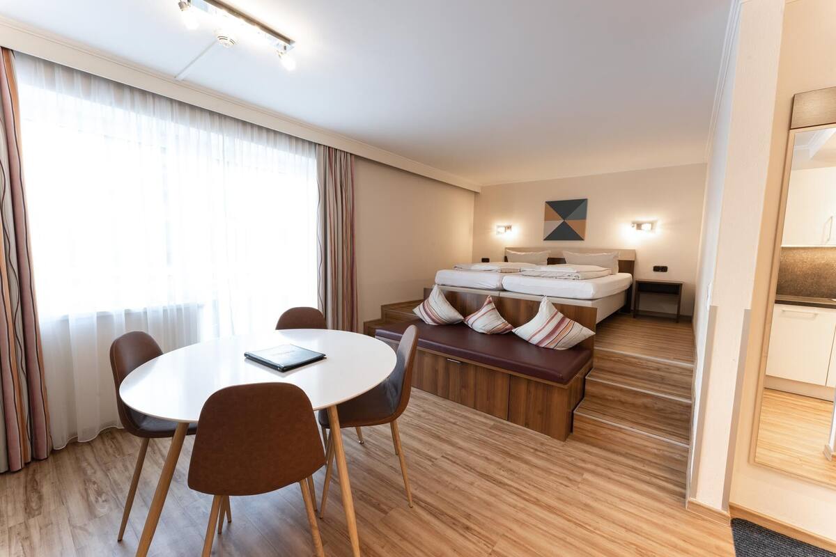 Quarto de hotel com área de jantar, sofá-cama e uma pequena cozinha equipada.