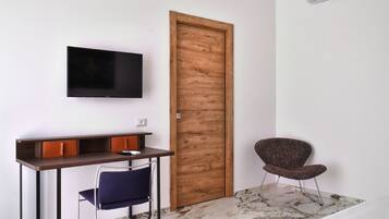 Quarto de hotel com porta de madeira, televisão na parede, secretária com cadeira e unidade de ar condicionado.