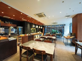 Interior de restaurante moderno com mesas de mármore, cadeiras de madeira, área de bar com máquina de Pepsi e grandes janelas com vista para o verde.