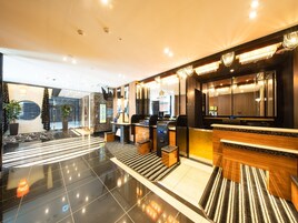 Um hall de hotel moderno com balcão de recepção, área de estar e um espelho grande refletindo o interior.