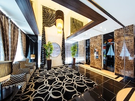 Um lobby moderno com carpete estampado em preto e branco, uma área de estar com sofás estampados, uma grande planta em vaso e uma parede de mármore.
