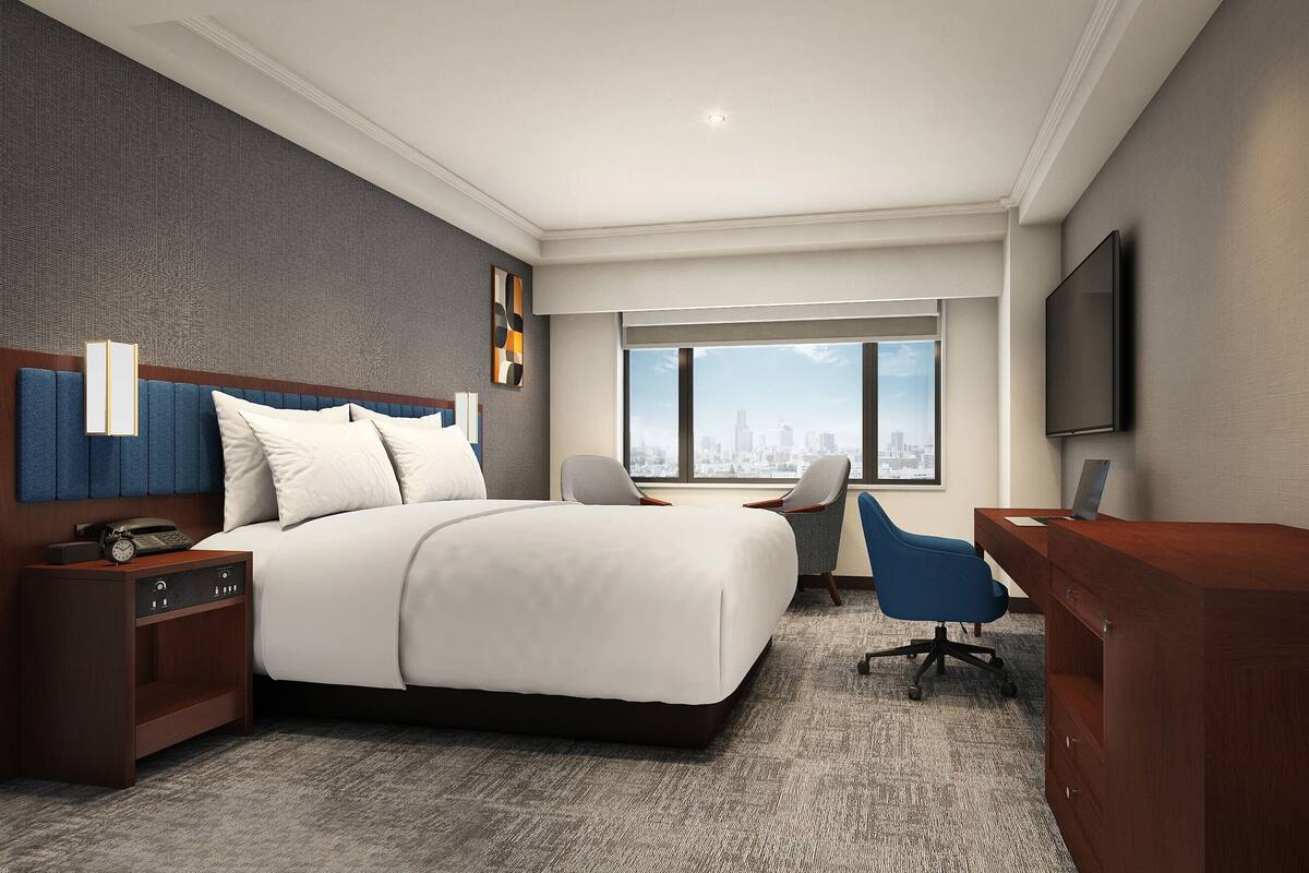 Quarto de hotel com cama, escrivaninha, cadeira, televisão e vista para a cidade.