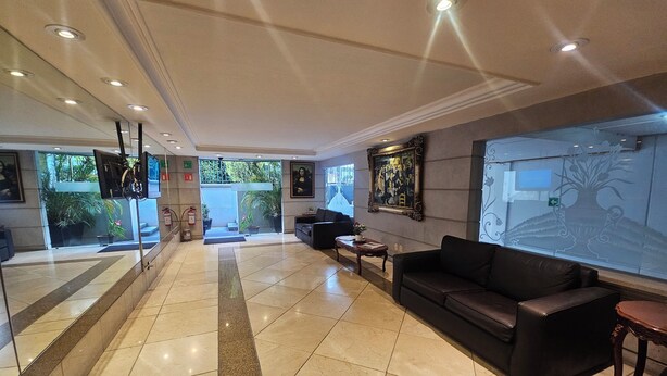 Um hall com piso de azulejos, um sofá de couro preto, uma mesa de centro e um quadro na parede.