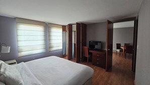 Quarto de hotel com uma cama grande, uma mesa de trabalho com cadeira, televisão e guarda-roupa.