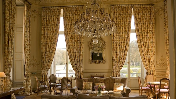 Uma sala imponente com um grande candelabro, cortinas elaboradas e um clássico conjunto de sofás.