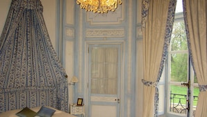 Quarto com cama de dossel, porta com painéis decorativos e vista para um jardim através de uma janela.