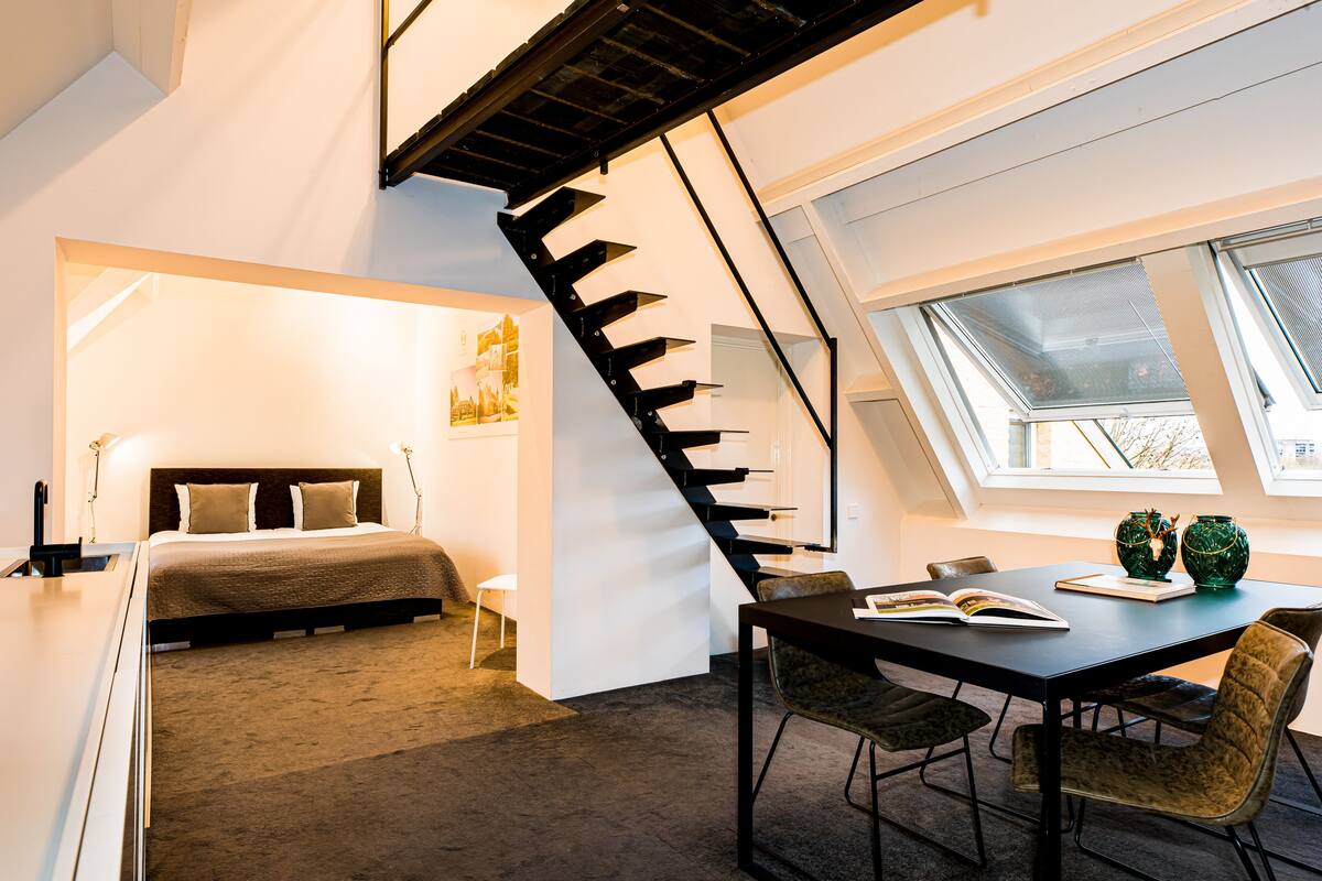 Quarto moderno com uma cama grande, uma escrivaninha com cadeiras e uma escada.
