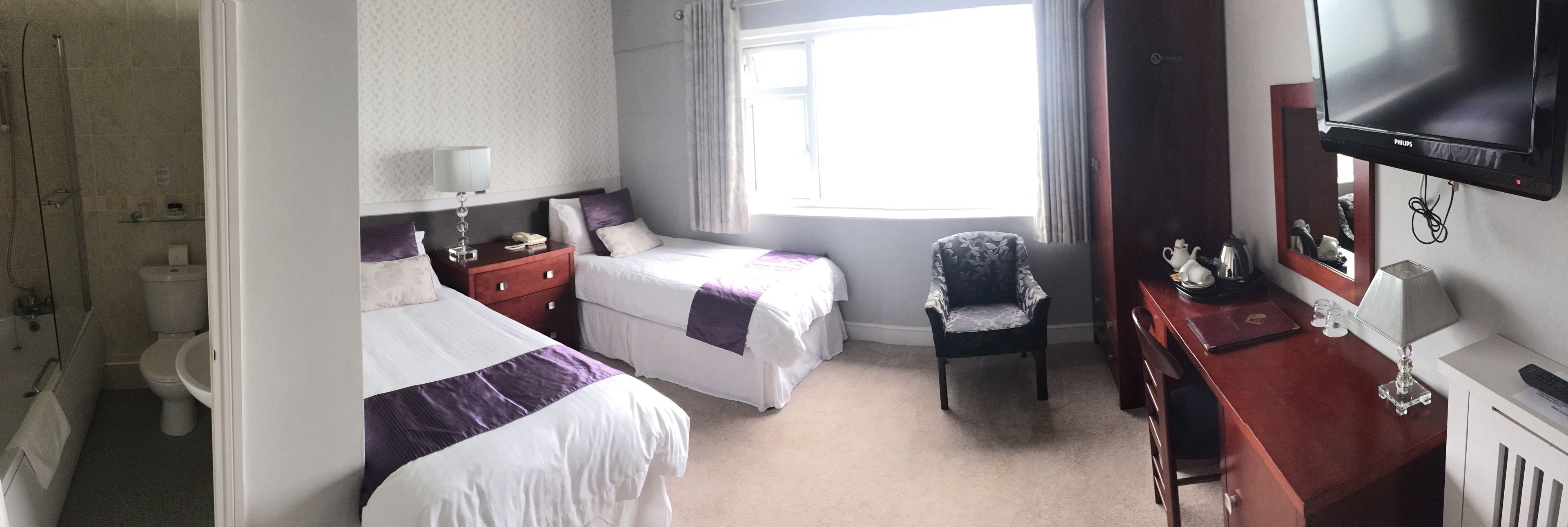 Quarto de hotel com duas camas, uma escrivaninha, uma cadeira, uma televisão e uma janela.