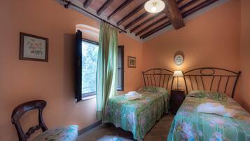 Quarto com duas camas, uma cadeira, janela com cortinas e um relógio de parede.