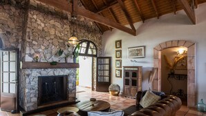 Lareira de pedra, sofá de couro e piso ladrilhado em uma sala de estar aconchegante.