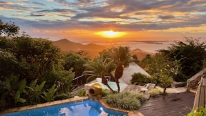Piscina com vista para o pôr do sol e montanhas.
