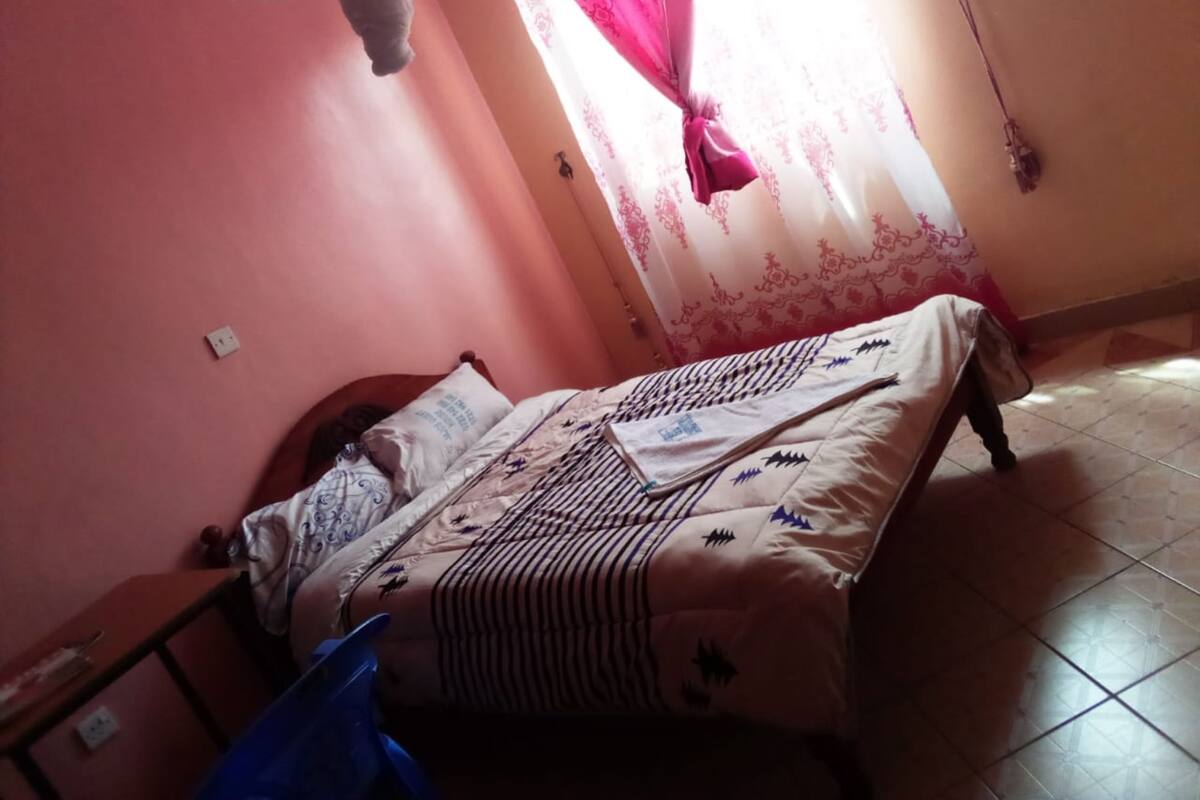 Quarto com cama, mesa de cabeceira e janela com cortinas.