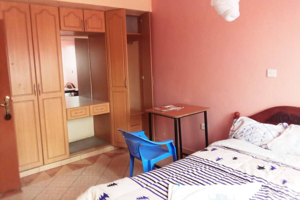 Um quarto com uma cama, uma escrivaninha, uma cadeira e um guarda-roupa.