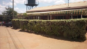 Um edifício com um reservatório de água no telhado, uma área de estar coberta ao ar livre e uma estrada de terra.