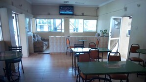 Uma sala de jantar com mesas, cadeiras, um sofá e uma televisão na parede.