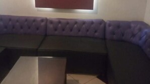 Quarto moderno com sofá em formato de L, uma mesa pequena e uma janela grande com um painel vermelho.